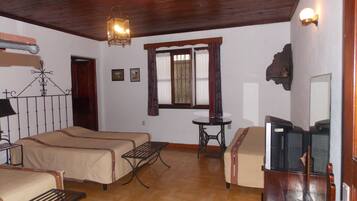 Quarto com duas camas, uma mesinha, uma cadeira, televisão e janela com cortinas.