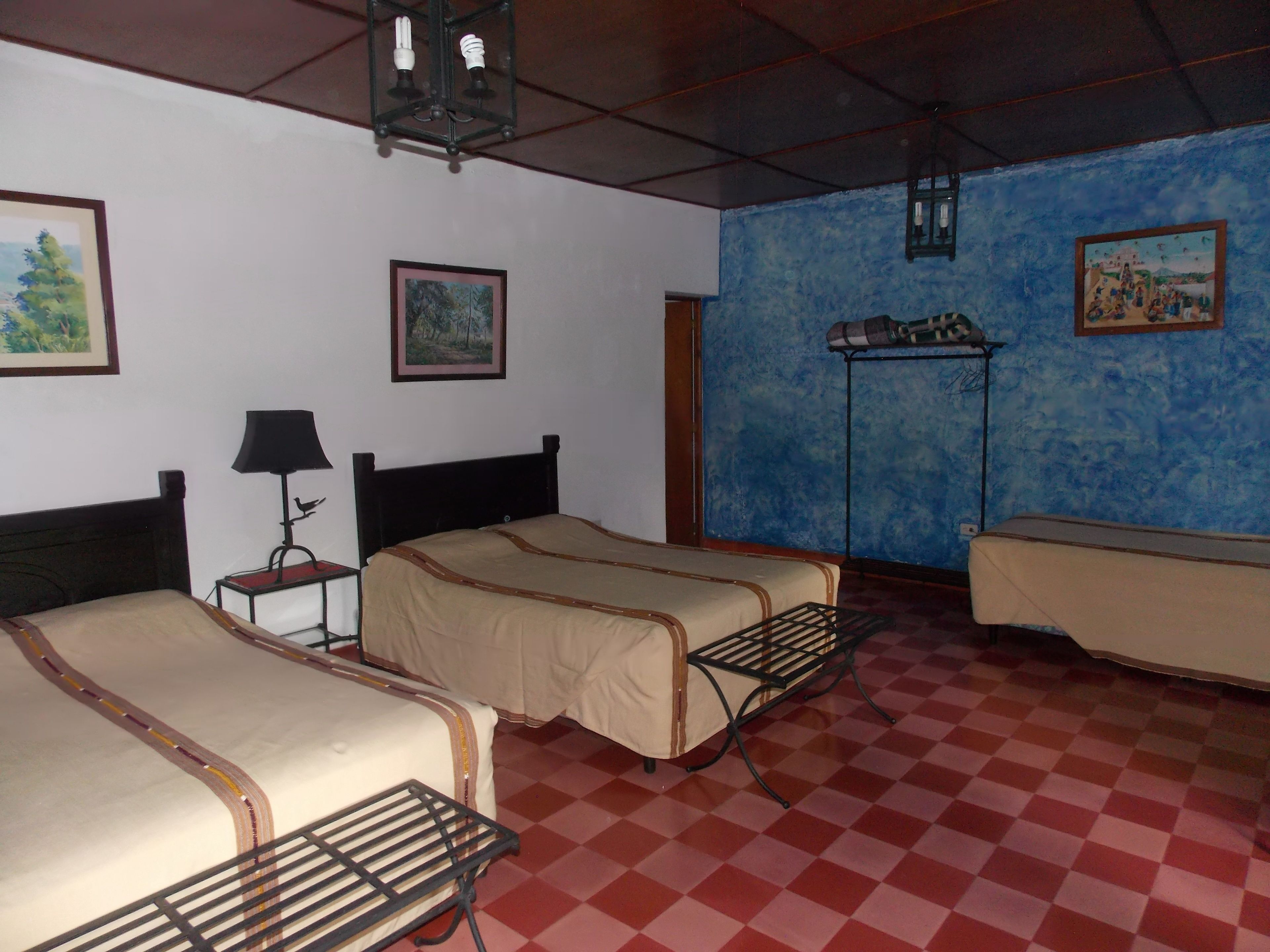 Quarto de hotel com duas camas, uma mesa de cabeceira, um abajur e uma parede com padrão texturizado azul.