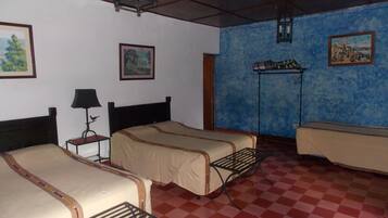 Quarto de hotel com duas camas, uma mesa de cabeceira, um abajur e uma parede com padrão texturizado azul.