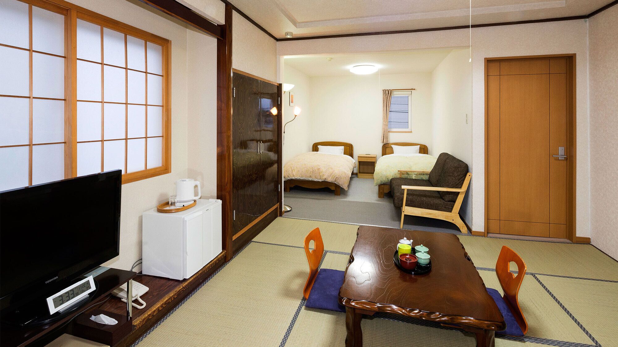 Um quarto japonês tradicional, com tatames, uma televisão, uma mesa de madeira com um conjunto de chá e duas camas.