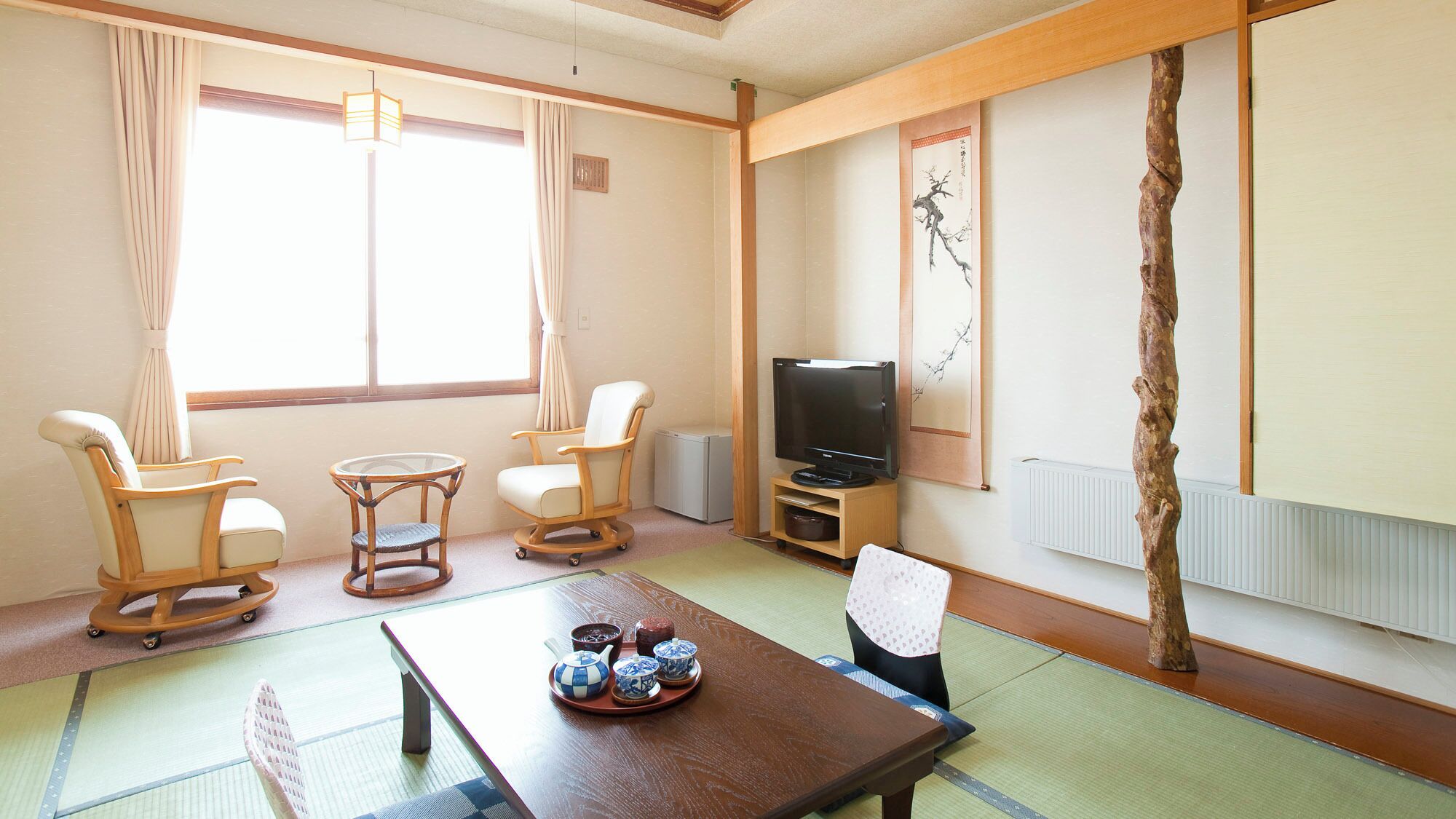 Quarto tradicional em estilo japonês, com piso de tatame, televisão e mesa de jantar posta com bules e xícaras.