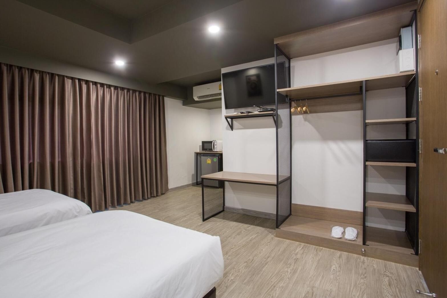 Quarto de hotel com duas camas, televisão em uma prateleira, pequeno espaço de cozinha e um guarda-roupa.