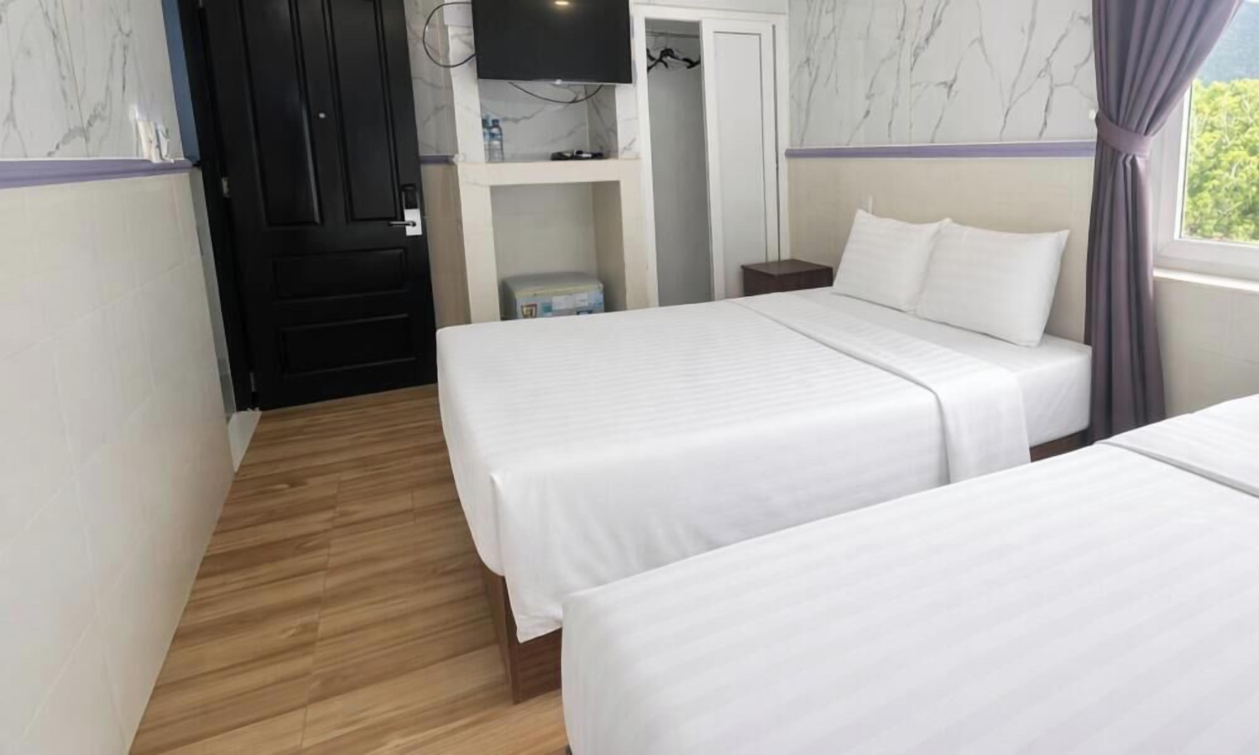 Quarto de hotel com duas camas, chão de madeira, televisão numa prateleira e um guarda-roupa.