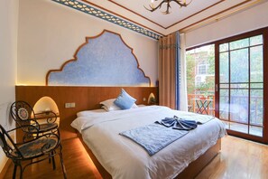 Quarto de hotel com uma cama grande, um candelabro, uma janela com vista para áreas verdes e um painel decorativo na parede.