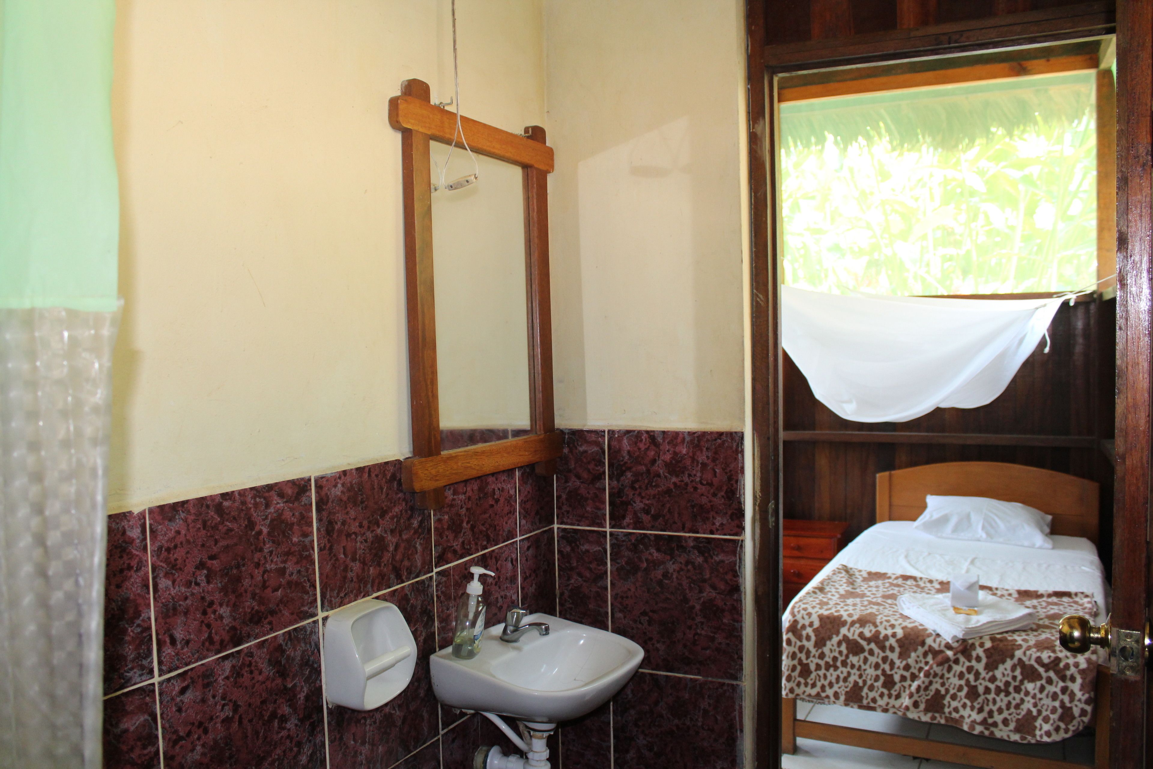 Casa de banho com parede revestida a mármore, lavatório branco com dispensador de sabonete e espelho com moldura de madeira.