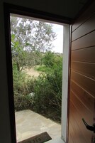 Uma porta dá acesso a um pátio com chão de pedra, rodeado por vegetação densa e árvores.
