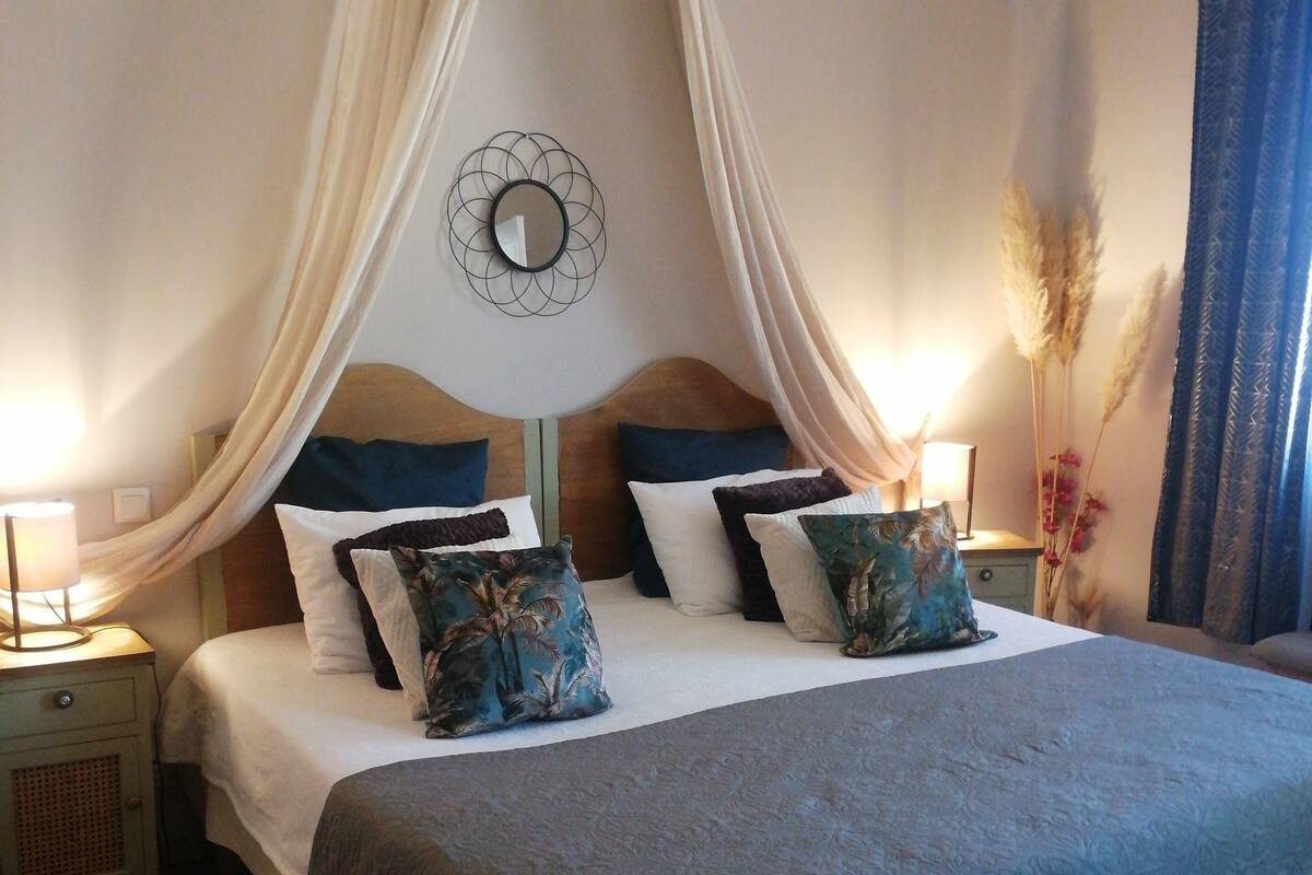 Quarto de hotel com uma cama de dossel, um tapete redondo e uma mesa de cabeceira com abajur.