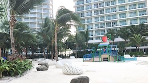 Pátio de hotel com palmeiras, parquinho e pedras grandes.