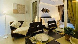 Quarto de hotel moderno com área de refeições, um sofá, uma mesa de jantar posta com pratos e copos, e um lustre.