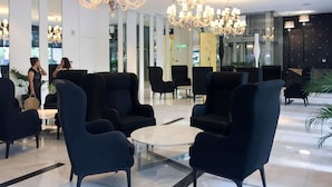 Um hall moderno com poltronas pretas, uma mesa redonda e vários candelabros.