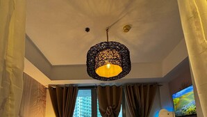 Um quarto com uma cama, luminária pendente, janela com cortinas e uma televisão na parede.