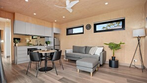 Um espaço de estar moderno com área de jantar, sofá cinzento e piso de madeira.