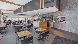 Um café moderno com mesas, cadeiras, um balcão e um barista, além de uma área de cozinha.