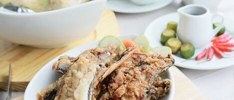 Uma mesa de jantar com uma tigela de sopa, um prato de frango frito e diversos acompanhamentos.