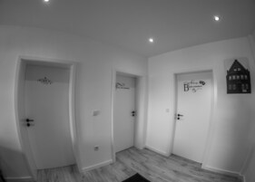 Um corredor com três portas, cada uma identificada com nomes e uma pequena decoração de casa.