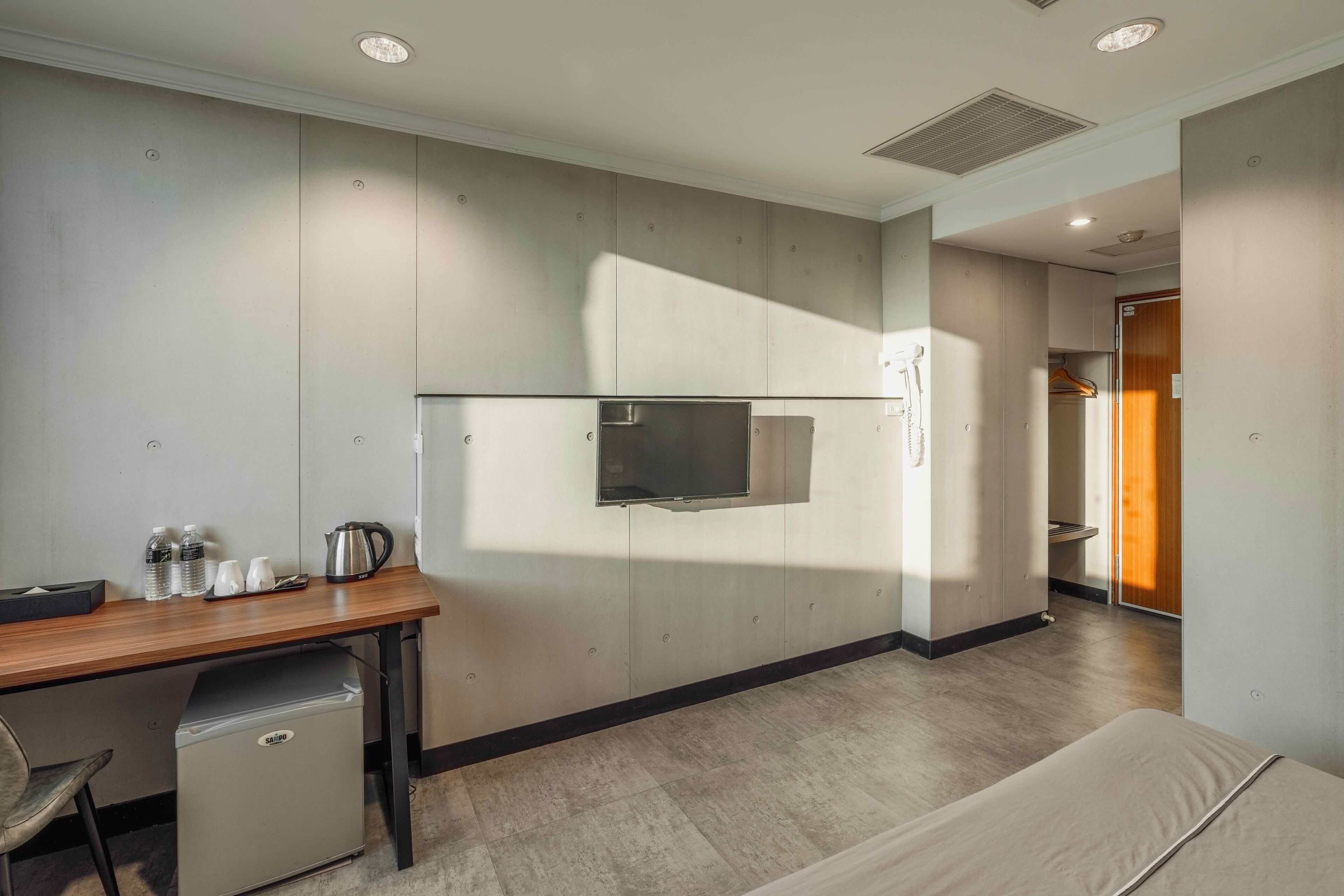 Quarto de hotel com cama, escrivaninha com cafeteira, televisão e mini-geladeira.