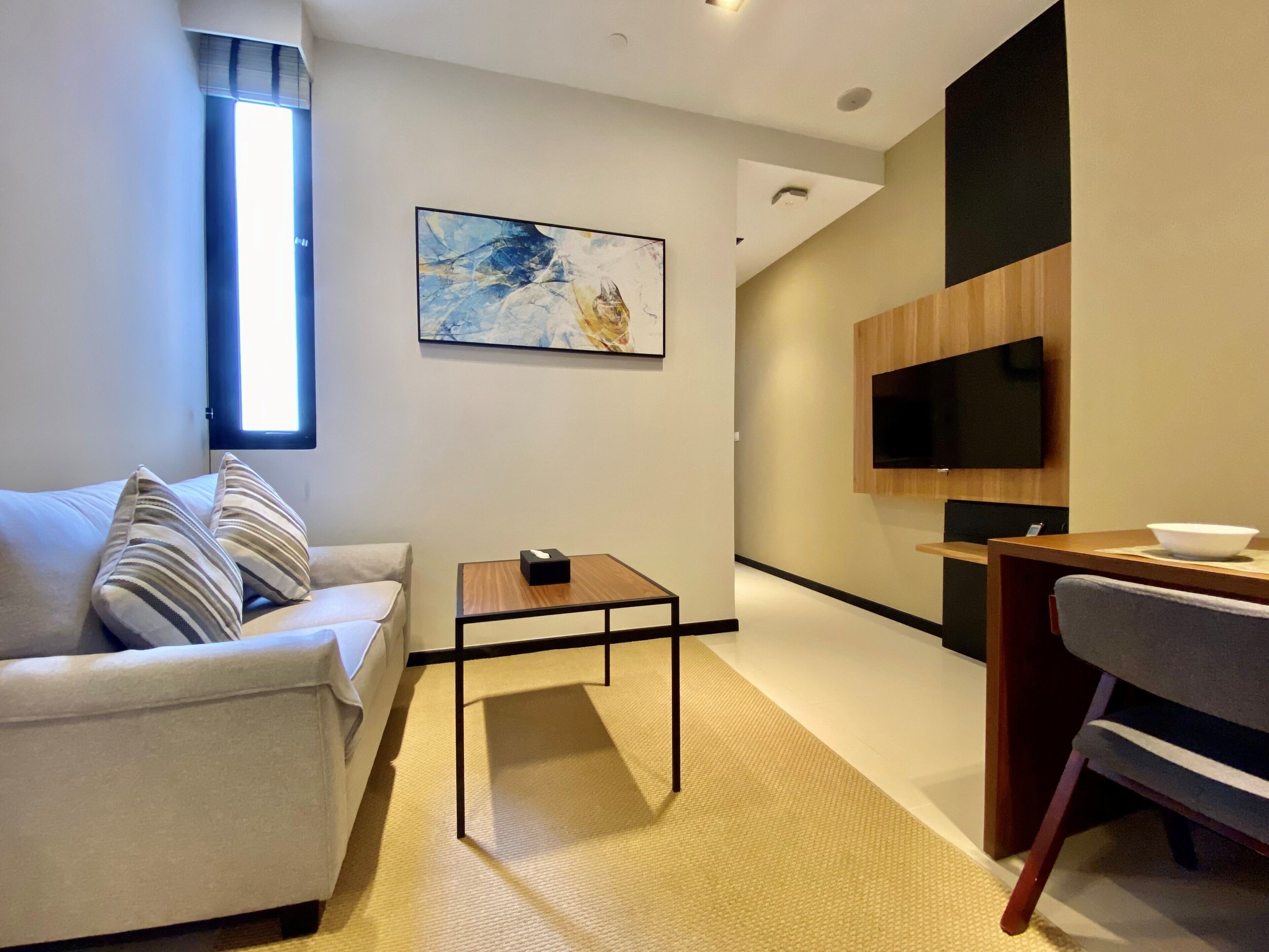 Uma sala de estar moderna com sofá, mesa de centro, TV na parede e área de jantar com mesa e cadeiras.