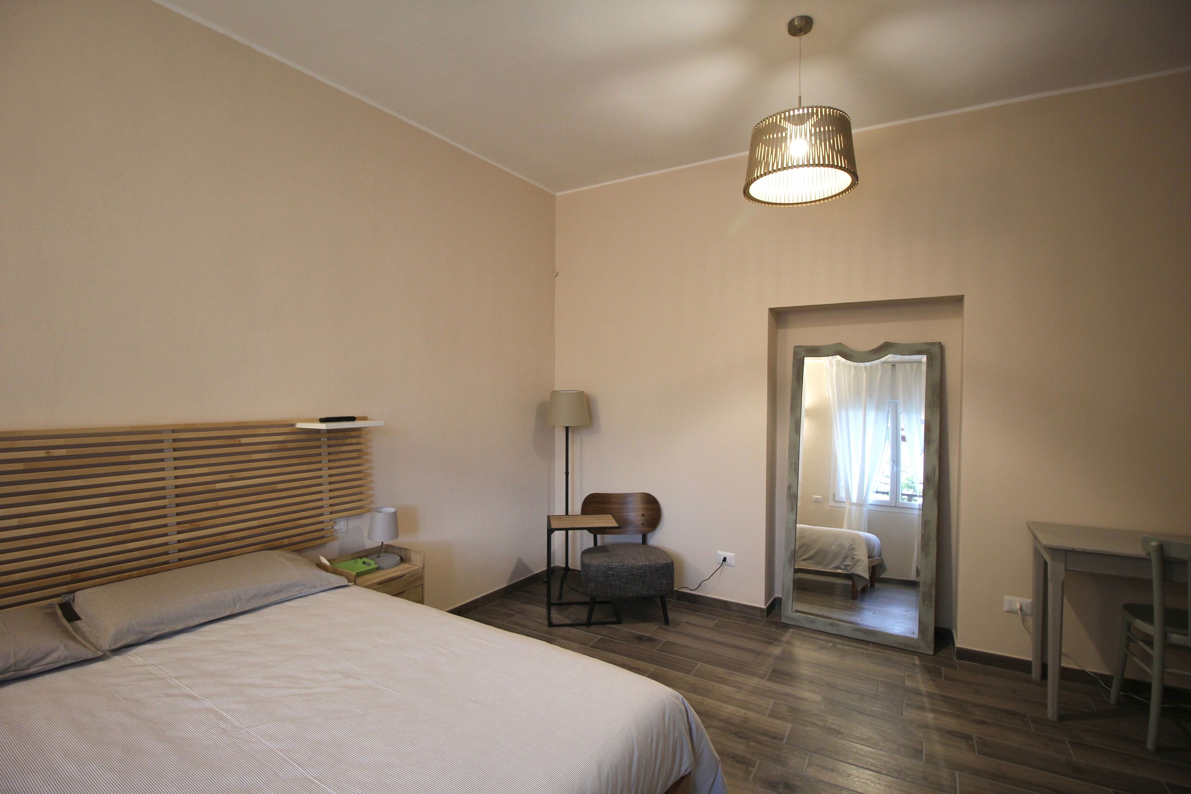 Quarto de hotel com cama, escrivaninha, cadeira, luminária e espelho.