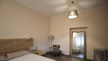 Quarto de hotel com cama, escrivaninha, cadeira, luminária e espelho.