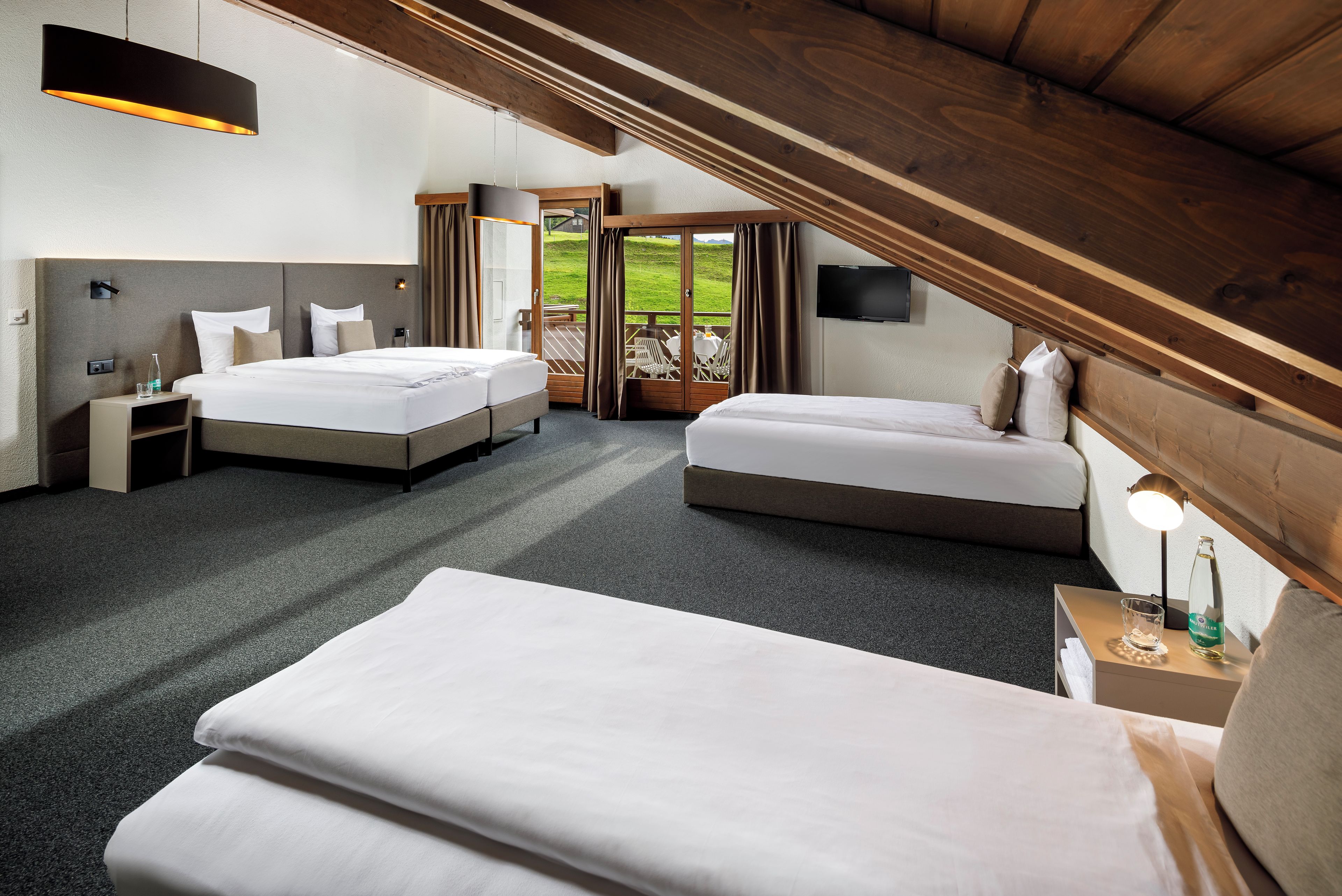 Quarto de hotel com duas camas, uma mesinha, um criado-mudo, uma TV e uma varanda com vista para o exterior.