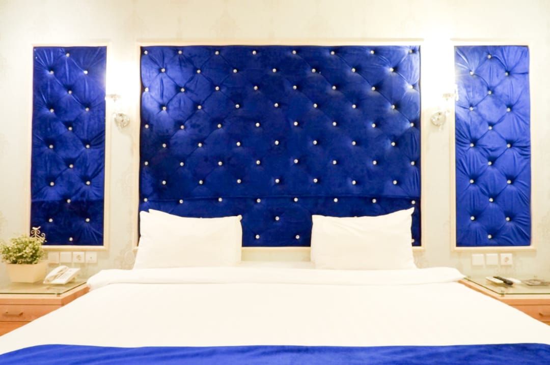 Quarto de hotel com uma cama grande, cabeceira estofada e mesa de cabeceira com abajur.