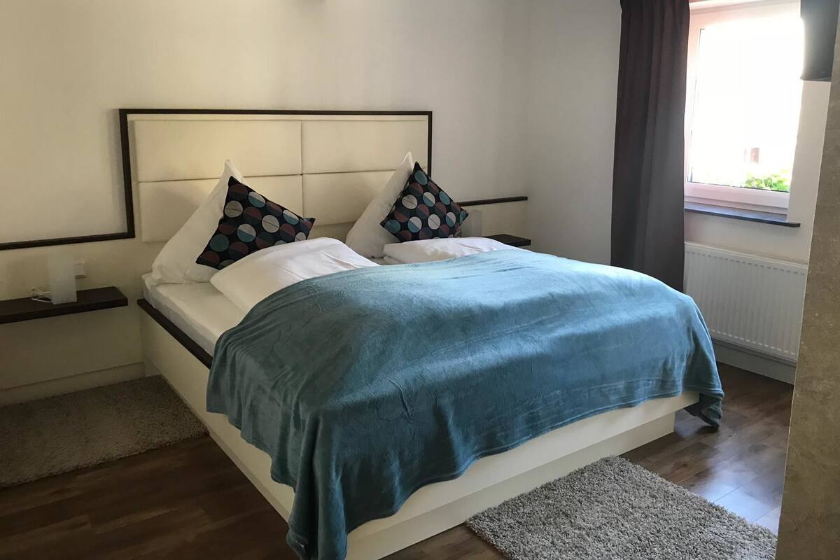 Quarto com cama, duas mesas de cabeceira, janela com cortinas e uma viga de madeira no teto.