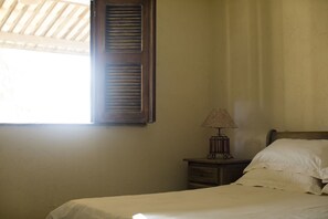 Um quarto com uma cama, mesa de cabeceira, abajur e janela com persianas.