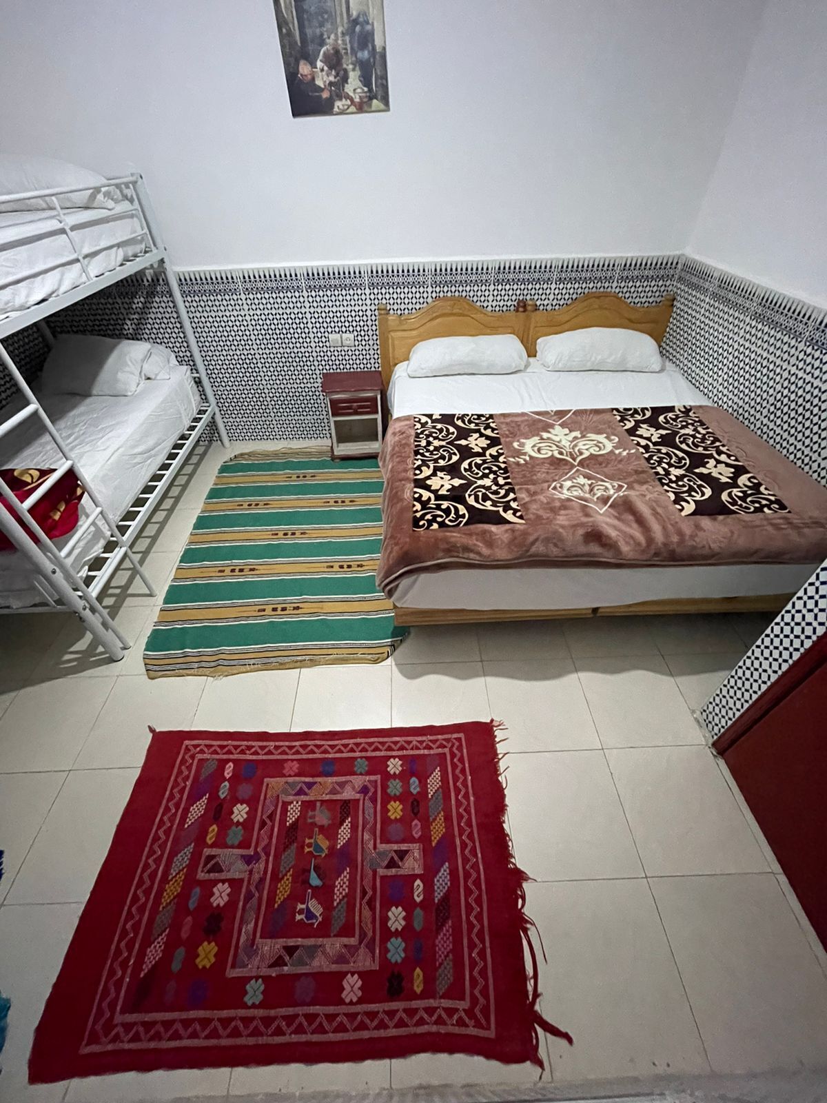 Quarto pequeno e compacto com uma beliche, uma cama de solteiro com manta estampada e dois tapetes.