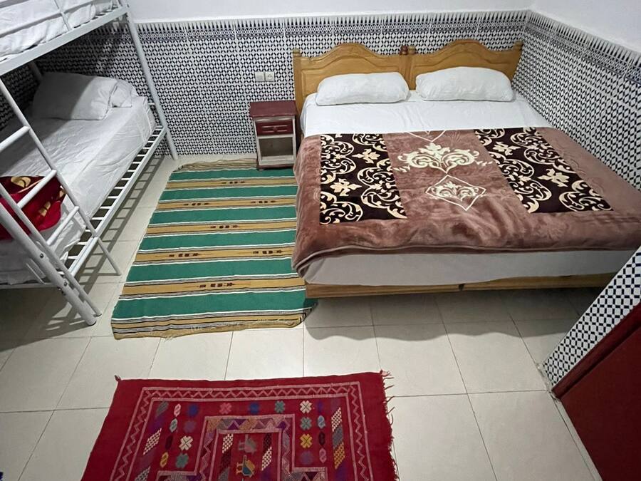 Quarto pequeno e compacto com uma beliche, uma cama de solteiro com manta estampada e dois tapetes.