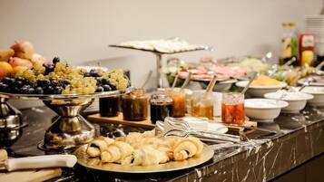 Buffet com diversos alimentos, incluindo frutas, doces e acompanhamentos.
