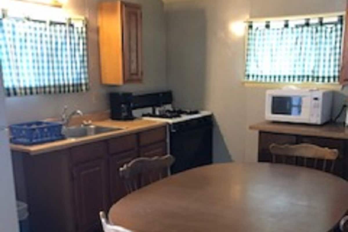 Cozinha compacta com armários de madeira, uma mesa de jantar redonda e um micro-ondas.