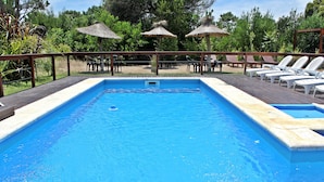 Piscina retangular com deck de madeira ao redor, com espreguiçadeiras e guarda-sóis de palha.