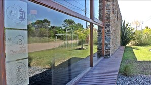 Um edifício moderno com grandes janelas de vidro refletindo um jardim e um céu claro.