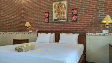 Quarto de hotel com parede de tijolos, cama com roupa de cama branca, cabeceira de madeira e duas luminárias de cabeceira.