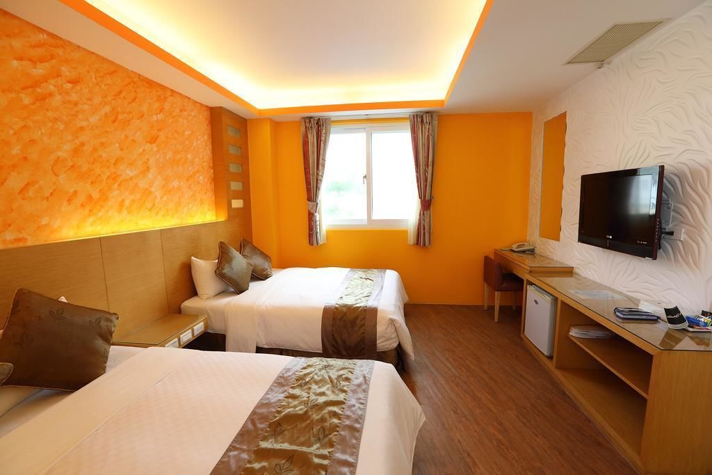Quarto de hotel com duas camas, uma escrivaninha, televisão e janela com cortinas.