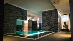Uma área de spa moderna com piscina em ambiente de vidro, paredes de pedra e uma estátua de Buda.