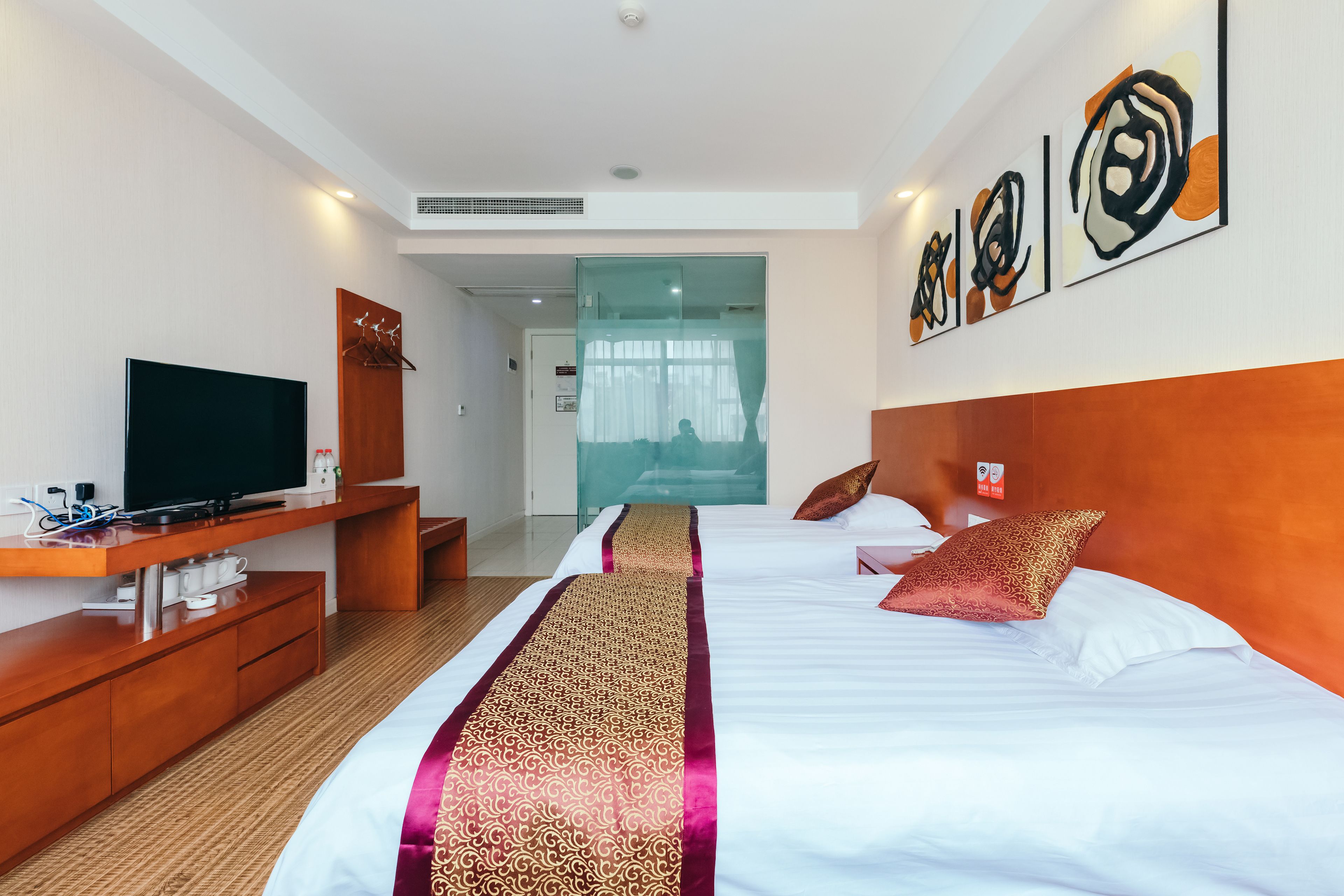 Quarto de hotel com duas camas, televisão, escrivaninha de madeira e obras de arte nas paredes.