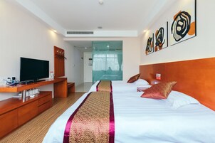 Quarto de hotel com duas camas, televisão, escrivaninha de madeira e obras de arte nas paredes.