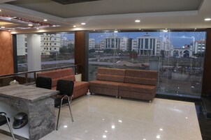 Um hall de hotel moderno com uma receção em mármore, assentos confortáveis e uma grande janela com vista para a paisagem urbana.