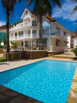 Um edifício de dois andares com varandas, piscina e palmeiras.
