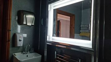 Casa de banho com lavatório branco, espelho iluminado e dispensador de sabonete.
