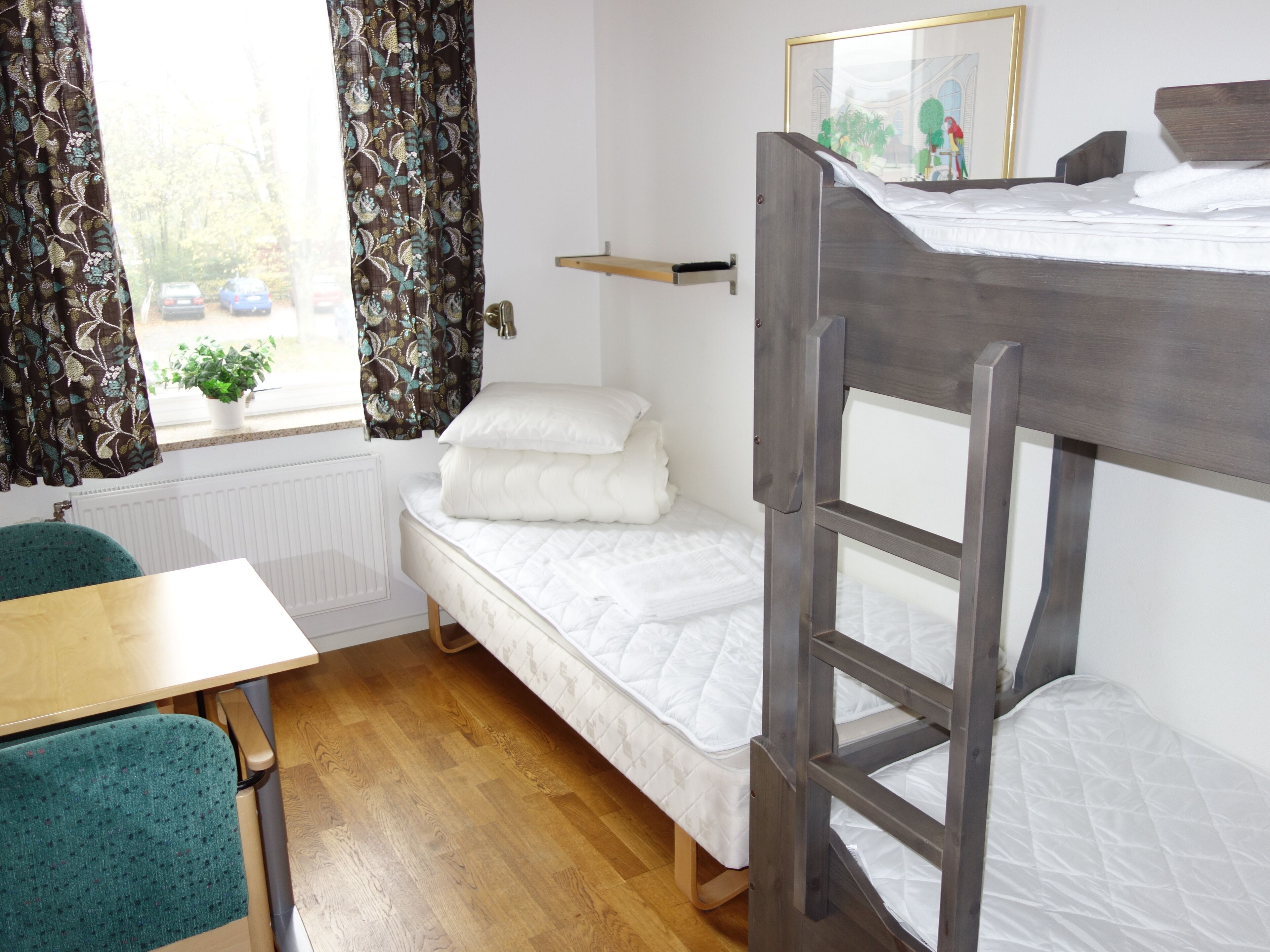 Quarto com beliche, escrivaninha e cadeira, janela com cortinas e radiador.