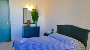 Quarto com cama, penteadeira, mesa de cabeceira, espelho e luminária na parede.