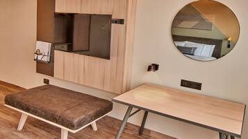 Quarto moderno com parede de painel de madeira, televisão montada, espelho redondo, pequena mesa e um banco.