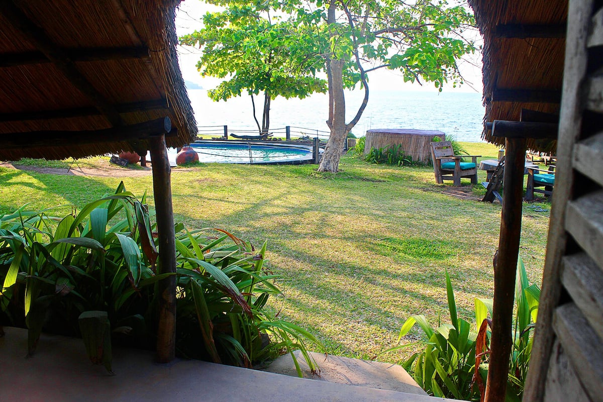 Área da piscina com vista para o mar, cercada por plantas tropicais e estruturas de madeira.