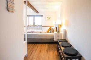 Quarto com cama, mesa de cabeceira, luminária e vista para o exterior.