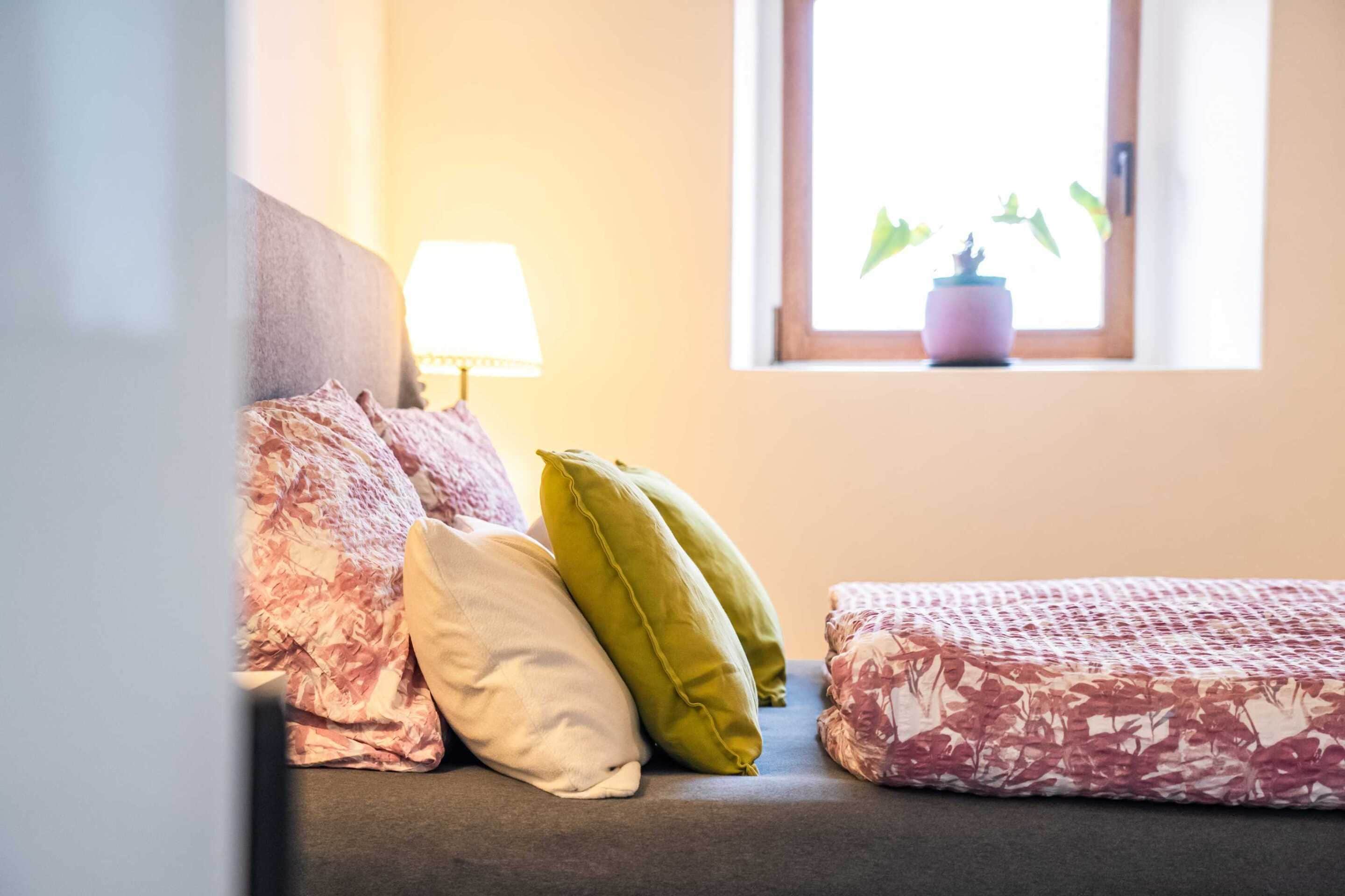 Uma cama com roupa de cama florida, um abajur e uma janela com uma planta.