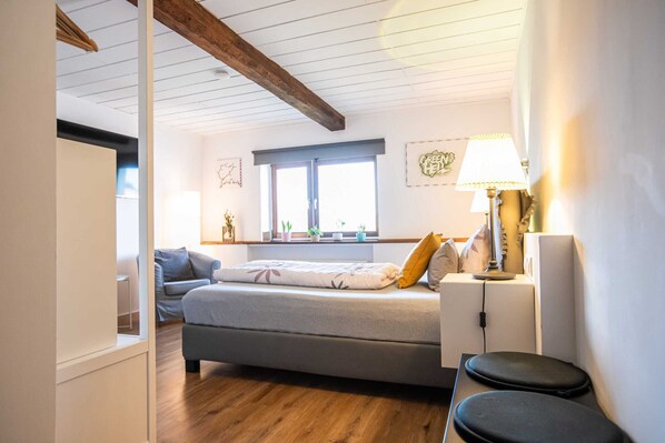 Quarto com cama, mesa de cabeceira, luminária e janela com plantas.