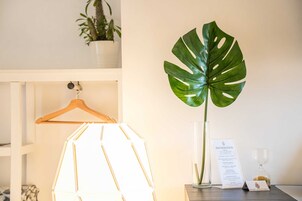 Quarto com luminária pendente, uma planta verde grande, um vaso de vidro e uma placa com informações.