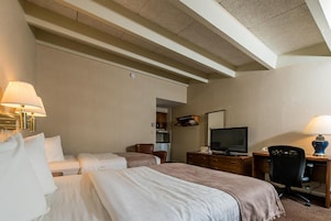 Quarto de hotel com duas camas, uma escrivaninha com computador, televisão e uma cadeira.